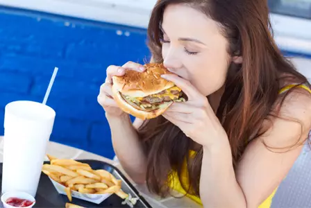 Žena jede masni hamburger i krumpiriće