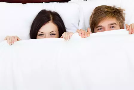 Man en vrouw verstoppen zich in bed onder dekens