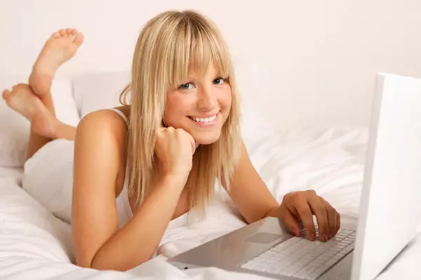 Млада жена на кревет со лаптоп